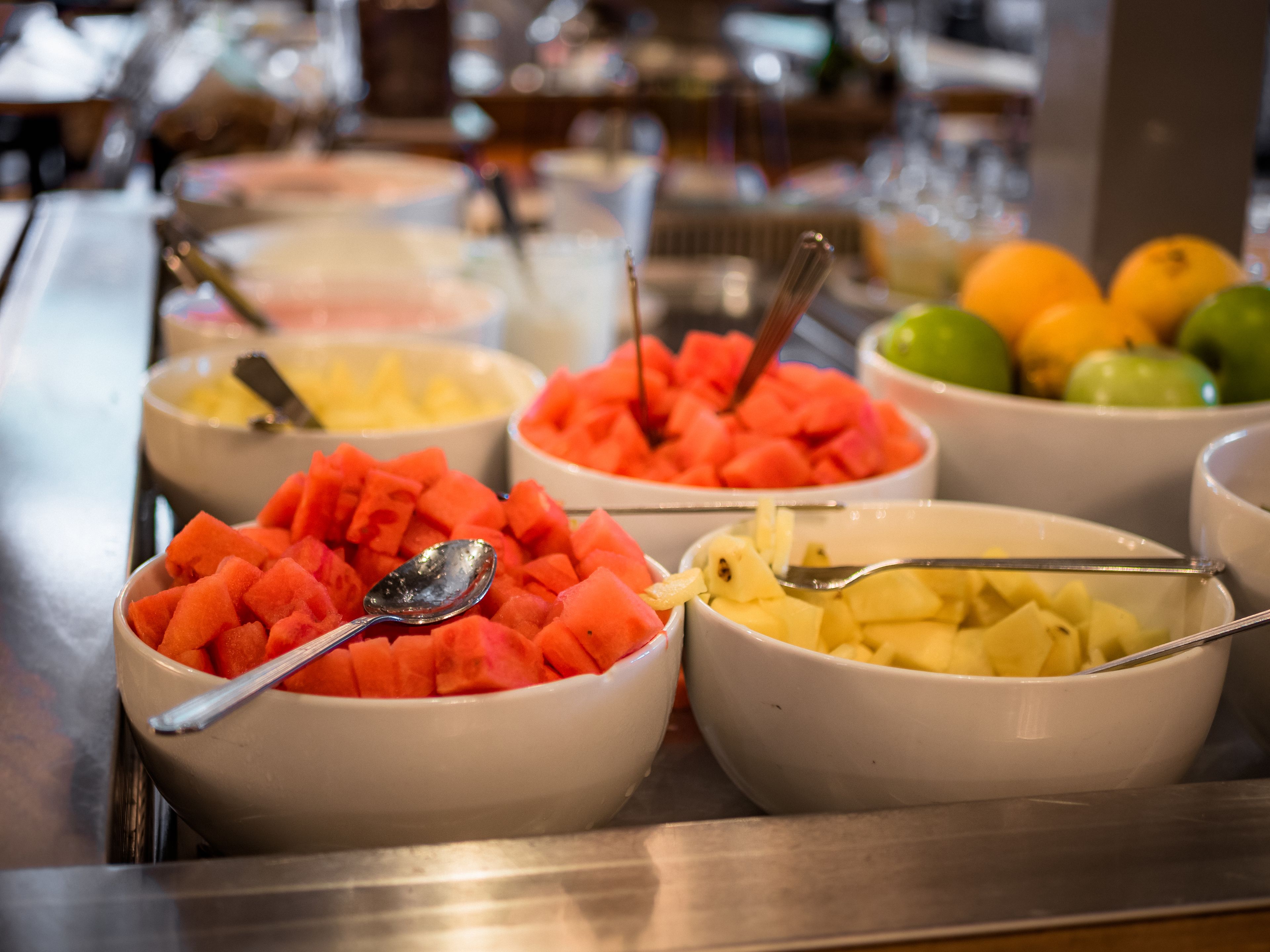 Buffet com diversas frutas e uma colher em cada recipiente.