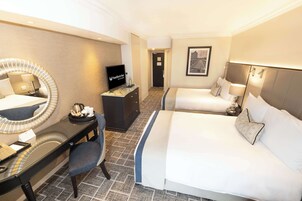 Quarto de hotel com uma cama, escrivaninha, cadeira e televisão.