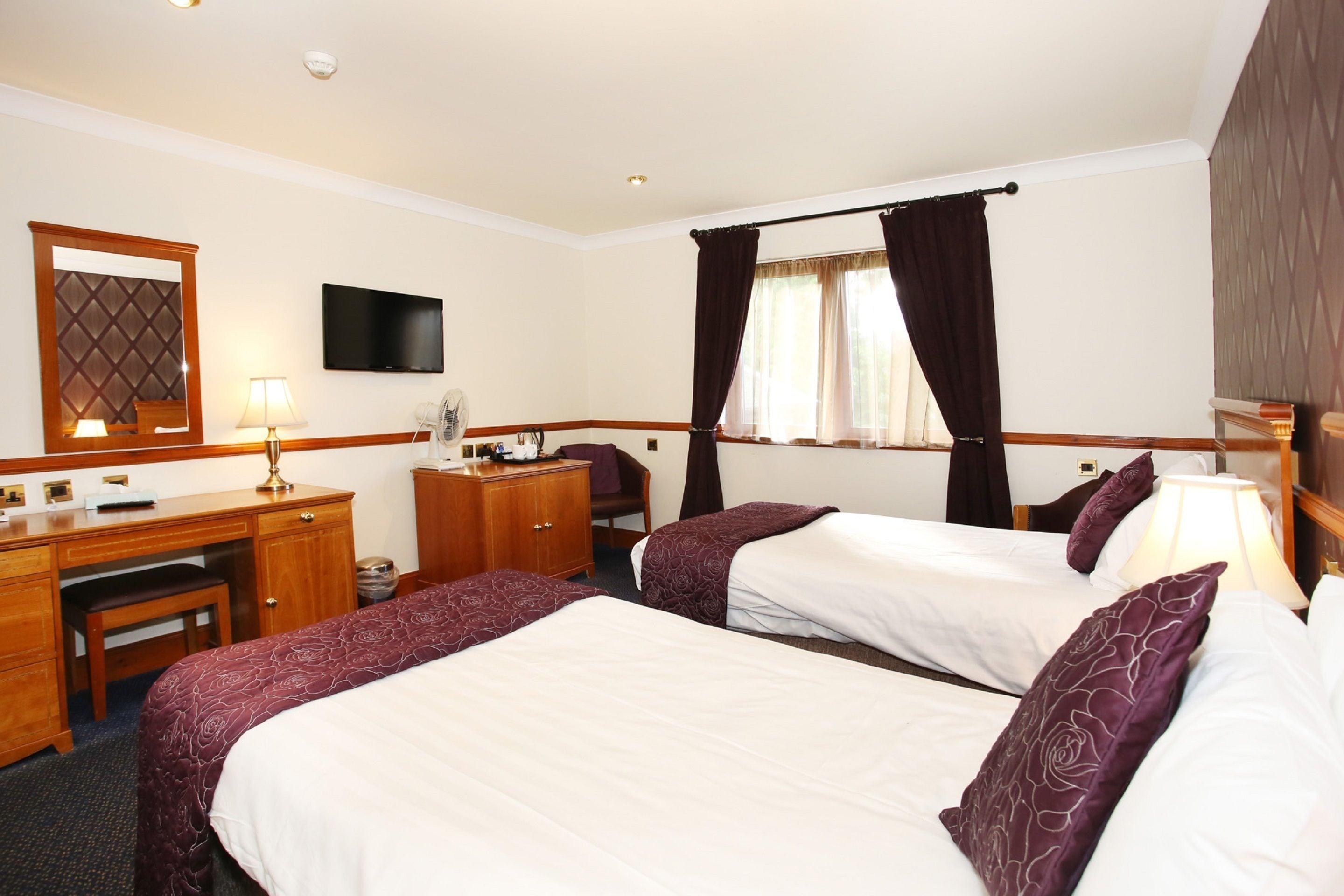 Quarto de hotel com duas camas, uma mesa, uma cadeira, uma televisão e uma janela com cortinas.