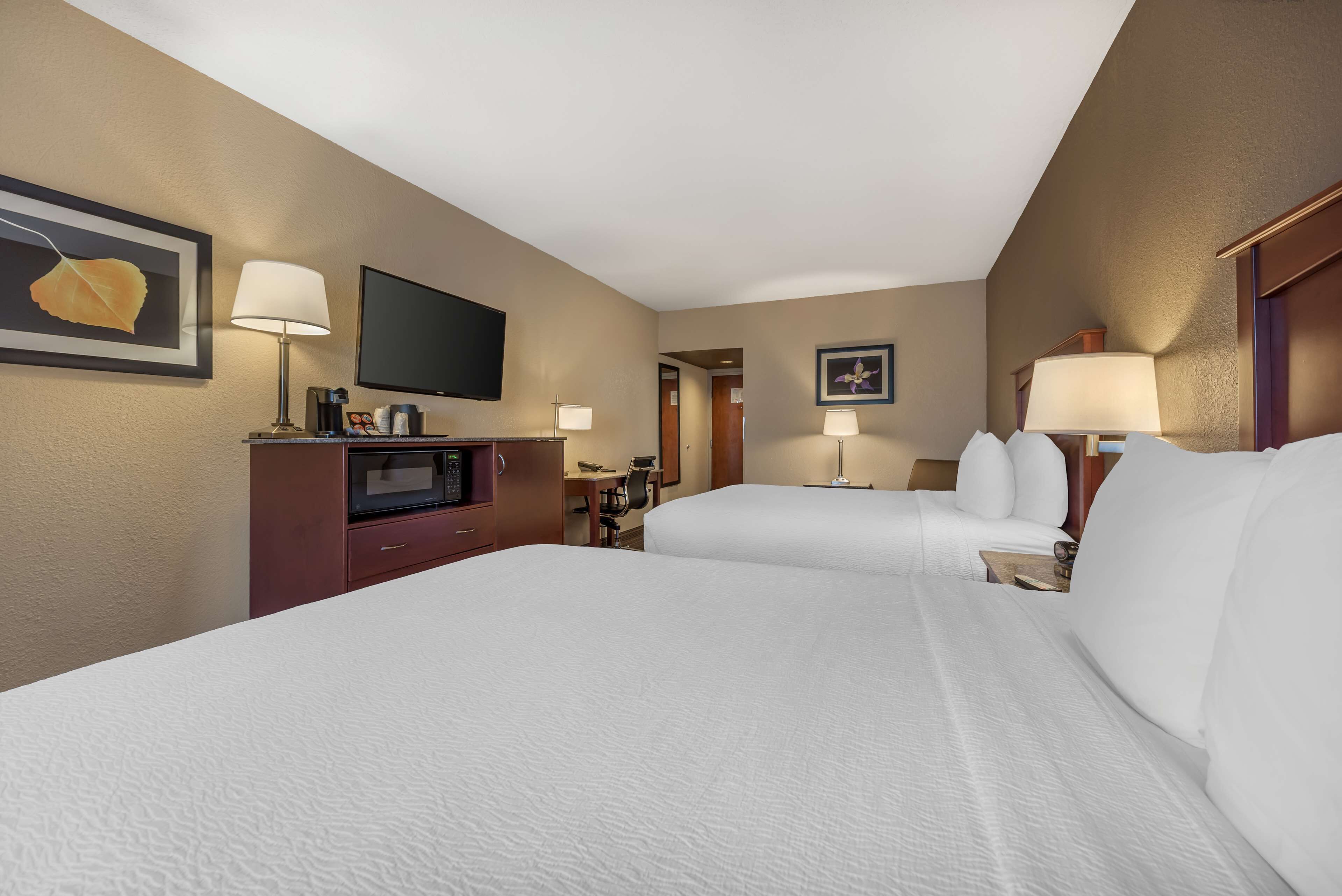 Quarto de hotel com duas camas, uma escrivaninha, televisão e máquina de café.
