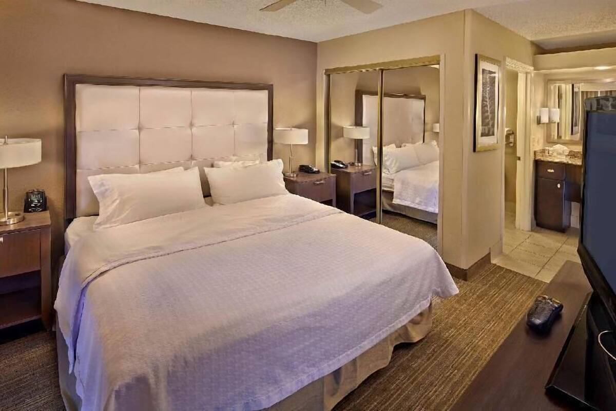 Quarto de hotel com uma cama grande, mesas de cabeceira, televisão e espelho.