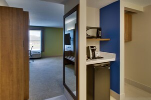 Quarto de hotel com porta de madeira, micro-ondas, máquina de café e pia pequena.