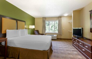 Quarto de hotel com uma cama grande, televisão, escrivaninha e janela com cortinas.