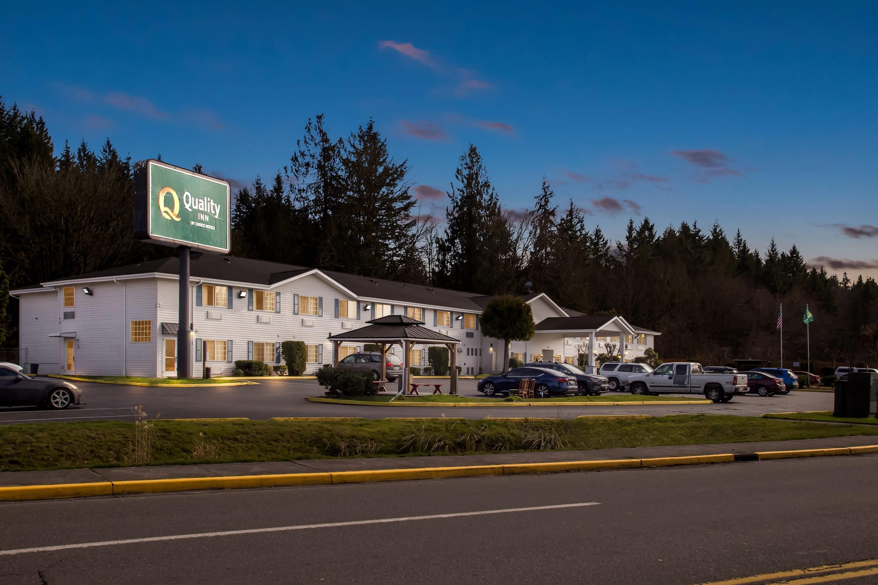 Um hotel Quality Inn com estacionamento, área de estar coberta ao ar livre e uma placa.