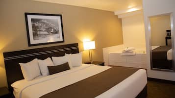 Quarto de hotel com uma cama grande, uma luminária de cabeceira, um quadro na parede, um banheiro com espelho e um porta-toalhas.