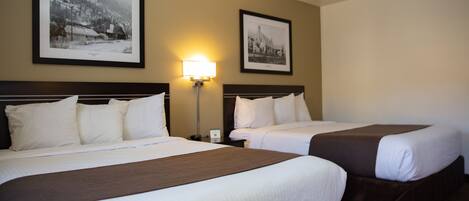 Quarto de hotel com duas camas, uma mesa de cabeceira, um abajur e duas imagens emolduradas na parede.