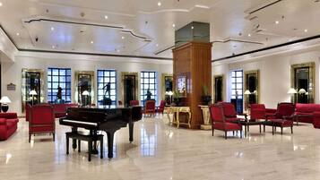 Um hall amplo com um piano de cauda, assentos vermelhos e grandes janelas.
