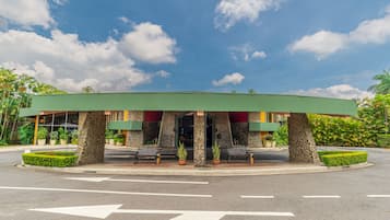 Entrada de hotel com toldo verde, pilares de pedra e bancos.