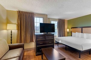 Quarto de hotel com cama, televisão em penteadeira, escrivaninha e sofá.