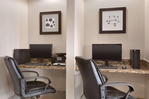 Um espaço de trabalho com escrivaninha, dois monitores, teclado, rato, impressora e cadeira.