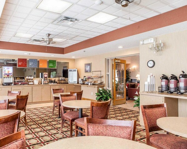 Um saguão de hotel com um balcão de café, área de estar e um relógio na parede.