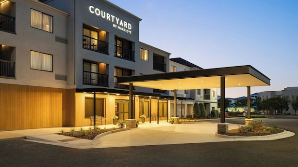 Um hotel Courtyard by Marriott com entrada coberta, área de estar externa e paisagismo.