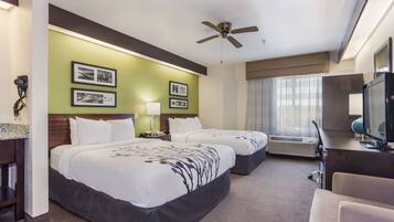 Quarto de hotel com duas camas, uma escrivaninha, televisão e ventoinha de teto.