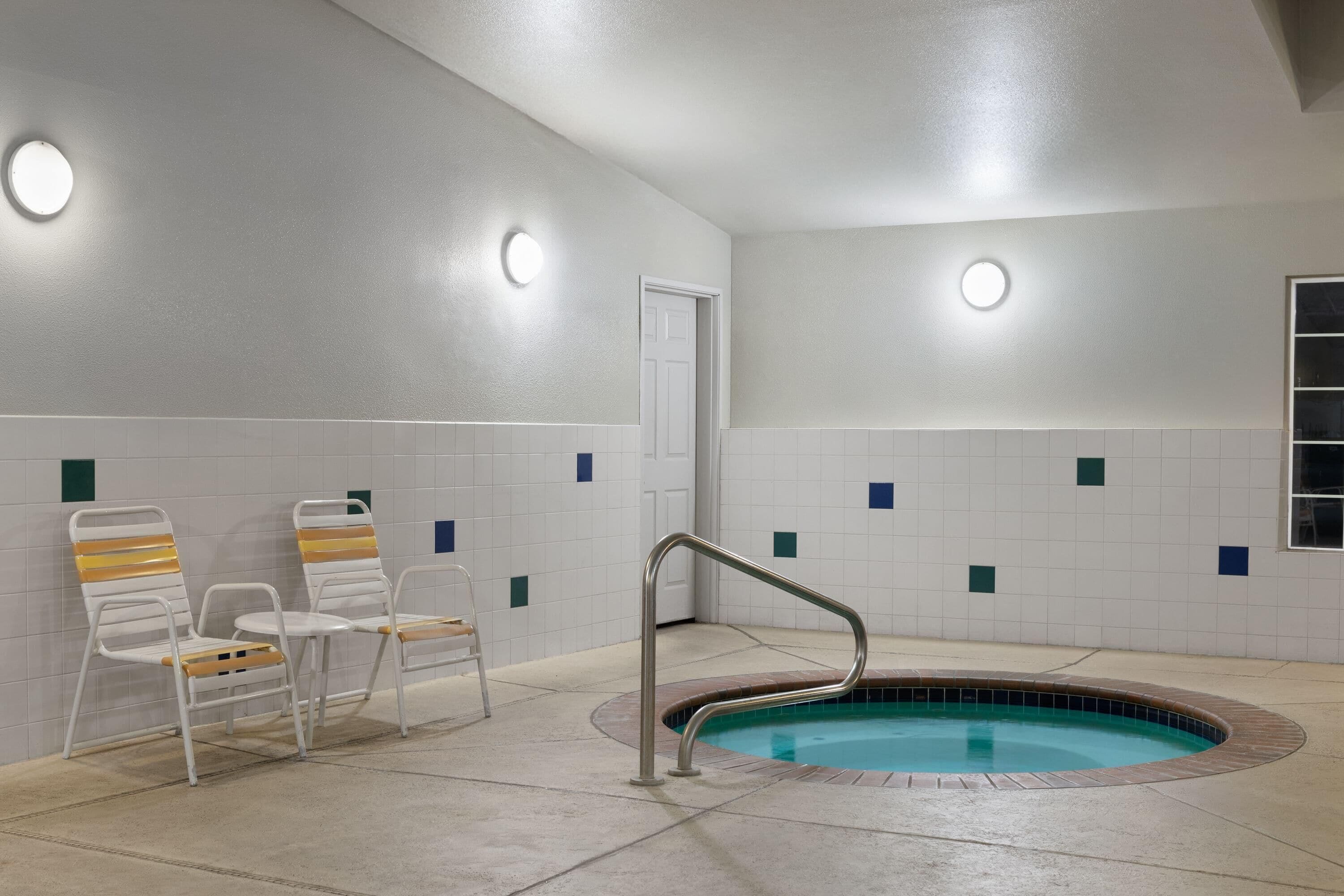Uma área de piscina com hidromassagem, assentos e uma porta.