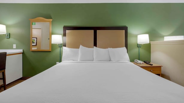 Quarto de hotel com uma cama grande, duas luminárias de cabeceira, uma mesa de cabeceira com telefone e um espelho na parede.