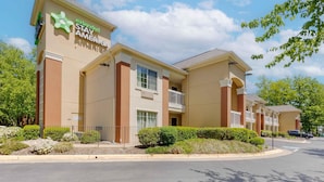 Um hotel com uma placa indicando 'extended STAY AMERICA', apresentando uma estrutura de dois andares com telhado plano, janelas amplas e um jardim frontal ajardinado.
