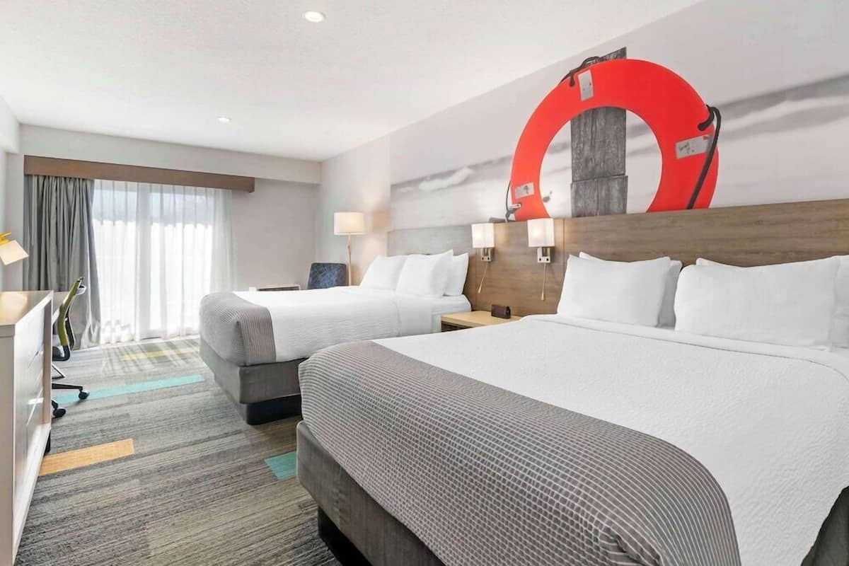 Quarto de hotel com duas camas, uma escrivaninha, uma cadeira e uma grande decoração circular na parede.