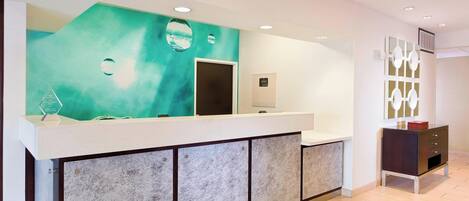Uma área de recepção com design moderno, com um espelho grande, um balcão de recepção e um pequeno espaço de estar com um armário.