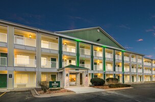 Um hotel de vários andares com um telhado verde, diversas varandas e uma placa indicando um escritório.