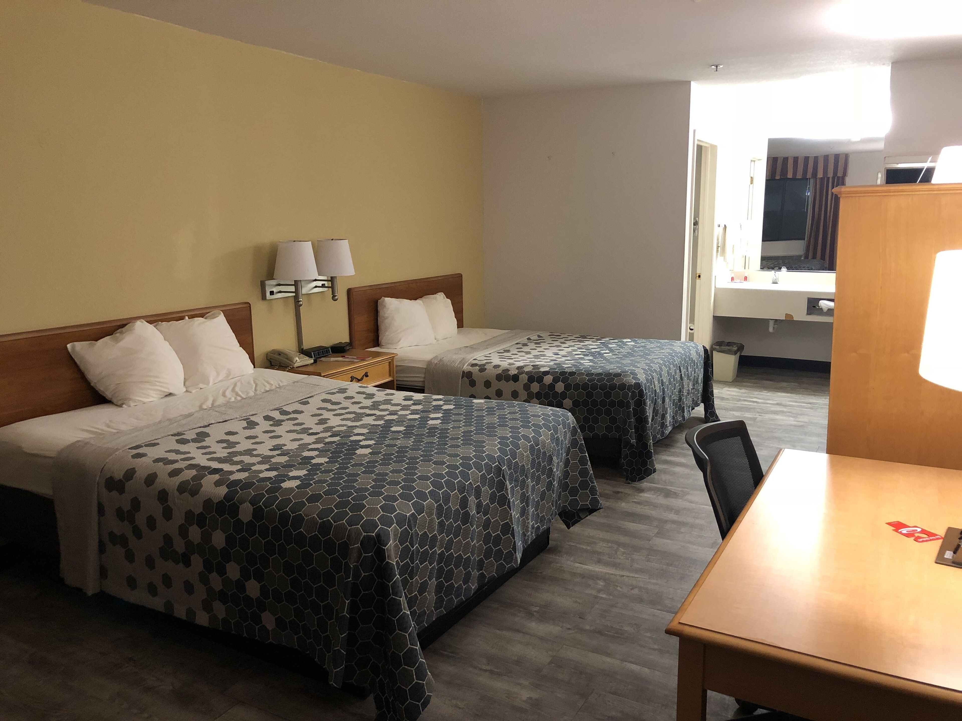 Quarto de hotel com duas camas, uma escrivaninha e uma cadeira. Há duas mesas de cabeceira com luminárias e um espelho.