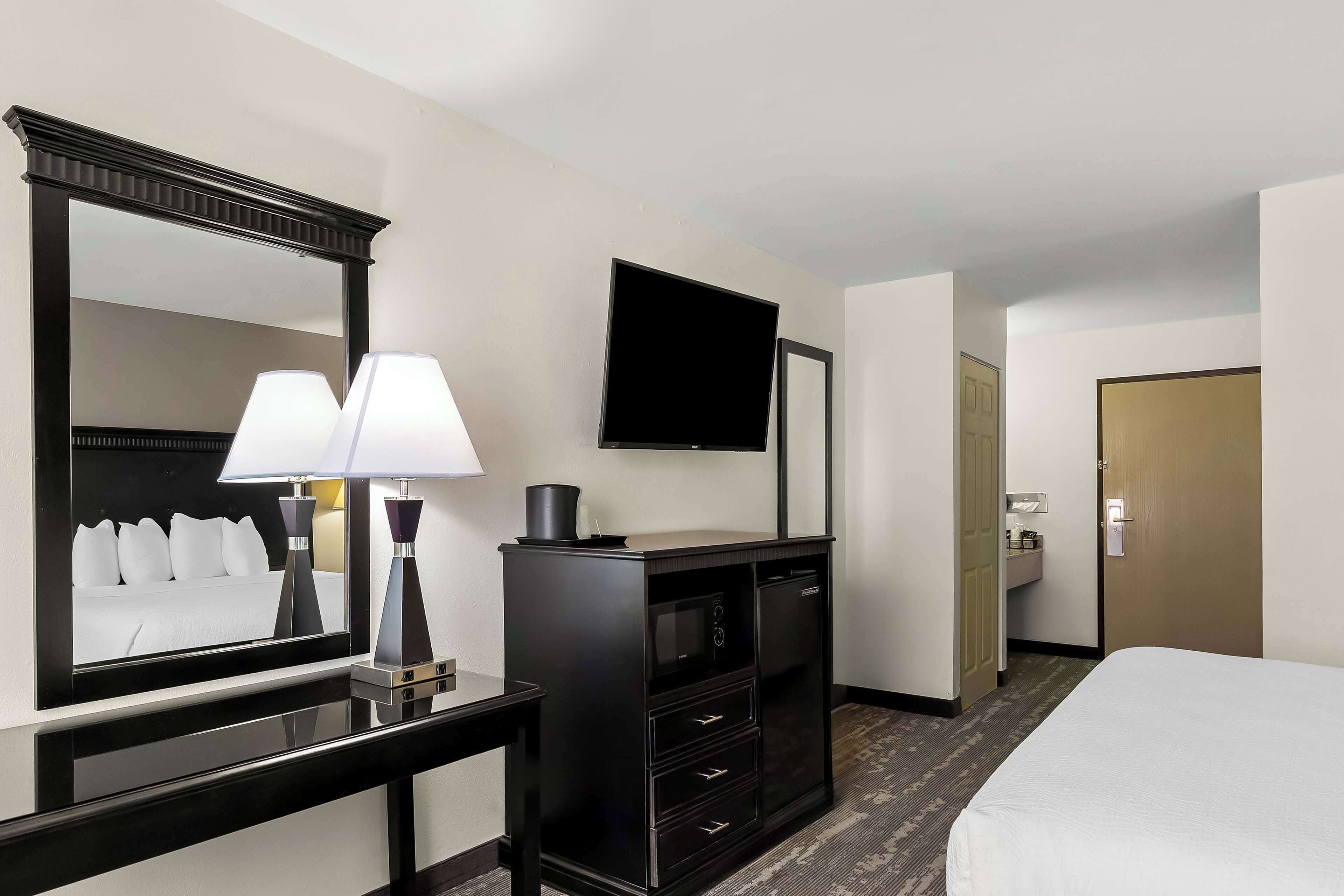 Quarto de hotel com uma cama, televisão, escrivaninha com luminária e penteadeira.