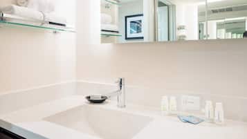 Uma casa de banho moderna com uma grande pia, prateleiras de vidro com toalhas, um espelho e produtos de higiene pessoal.