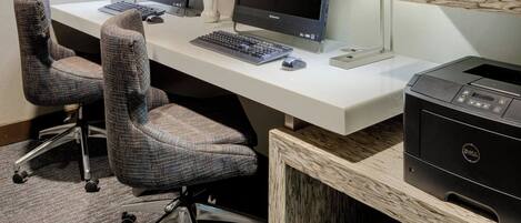 Um espaço de escritório moderno com duas mesas, cadeiras, computadores, uma impressora e objetos decorativos.