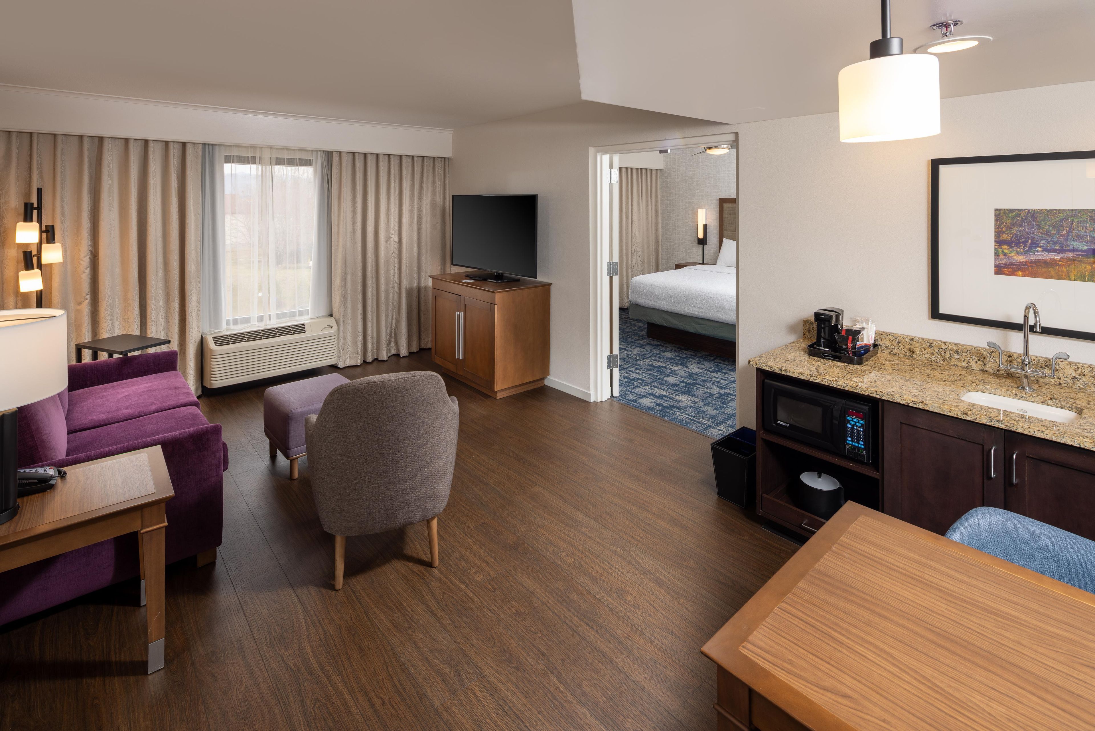Quarto de hotel com cama, televisão, escrivaninha, cadeira, cafeteira e banheiro com pia e espelho.