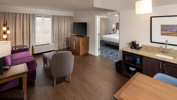 Quarto de hotel com cama, televisão, escrivaninha, cadeira, cafeteira e banheiro com pia e espelho.
