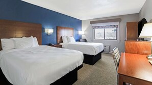 Quarto de hotel com duas camas, uma escrivaninha e uma janela com vista.