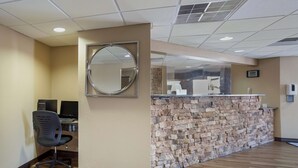 Uma área de recepção com parede de pedra, um espelho redondo, um balcão de atendimento e um computador.