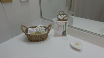 Uma casa de banho com uma pia branca, uma cesta de vime com artigos de higiene e um folheto de spa no balcão.