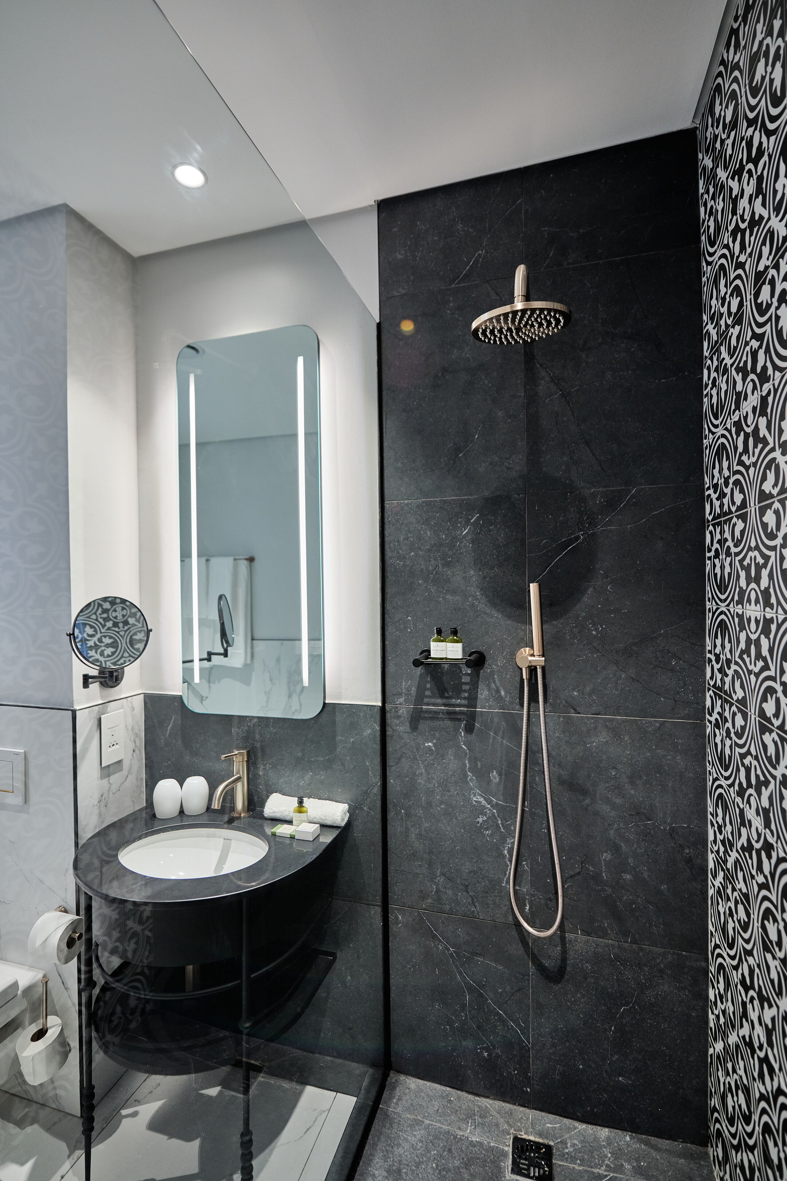 Uma casa de banho moderna com lavatório de mármore preto, um espelho grande e chuveiro com cabeça de duche manual.