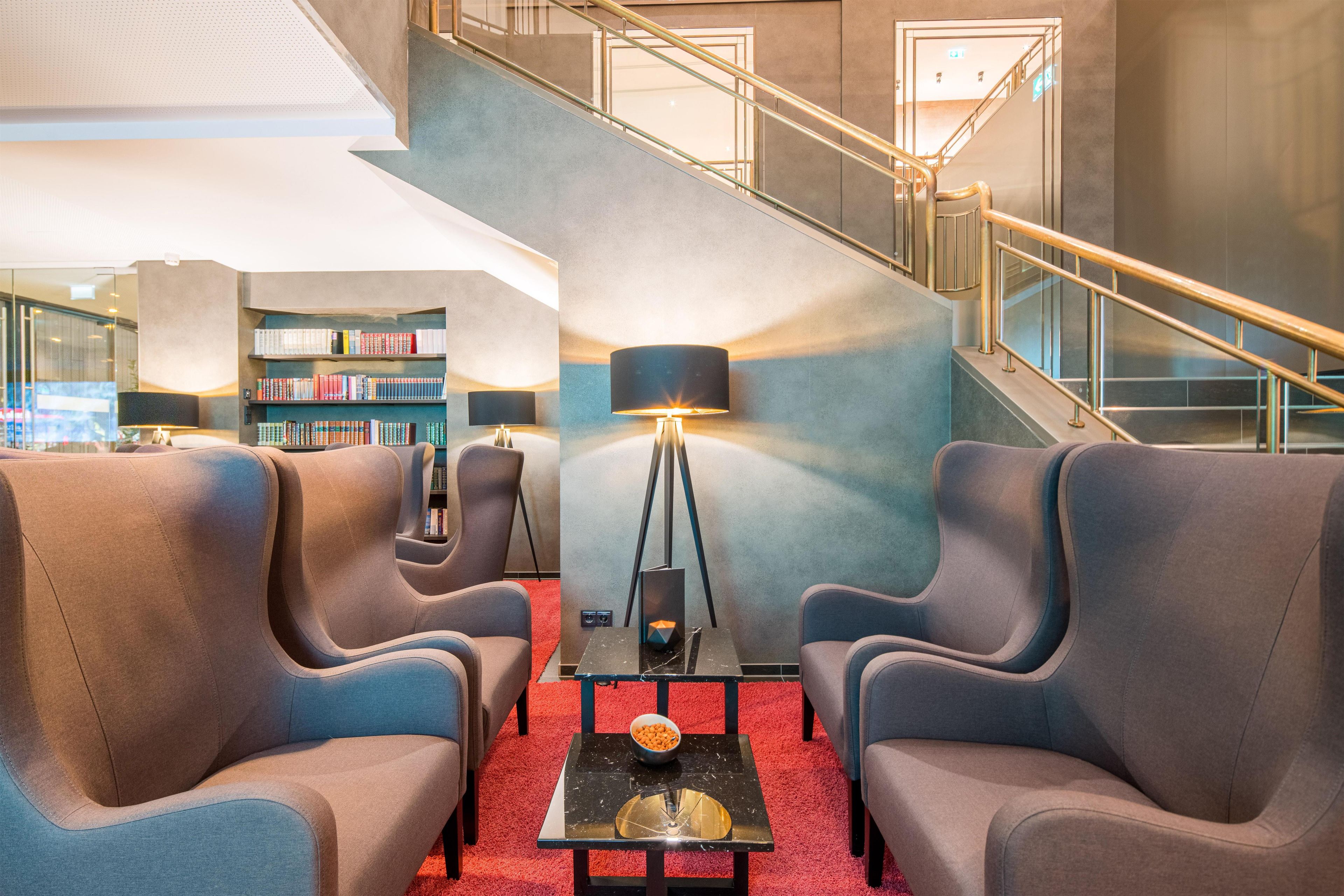 Um lobby moderno com escada, área de estar e estante de livros.