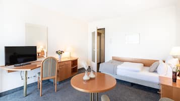 Quarto de hotel com cama, escrivaninha com televisão, poltrona, mesa redonda e sofá.