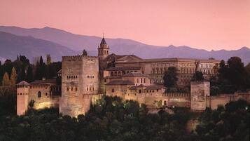 Um complexo de castelo histórico com várias torres e um edifício grande, rodeado por montanhas e árvores.