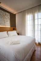 Uma cama grande e bem arrumada com lençóis brancos, cabeceira de madeira e parede de destaque em mármore.