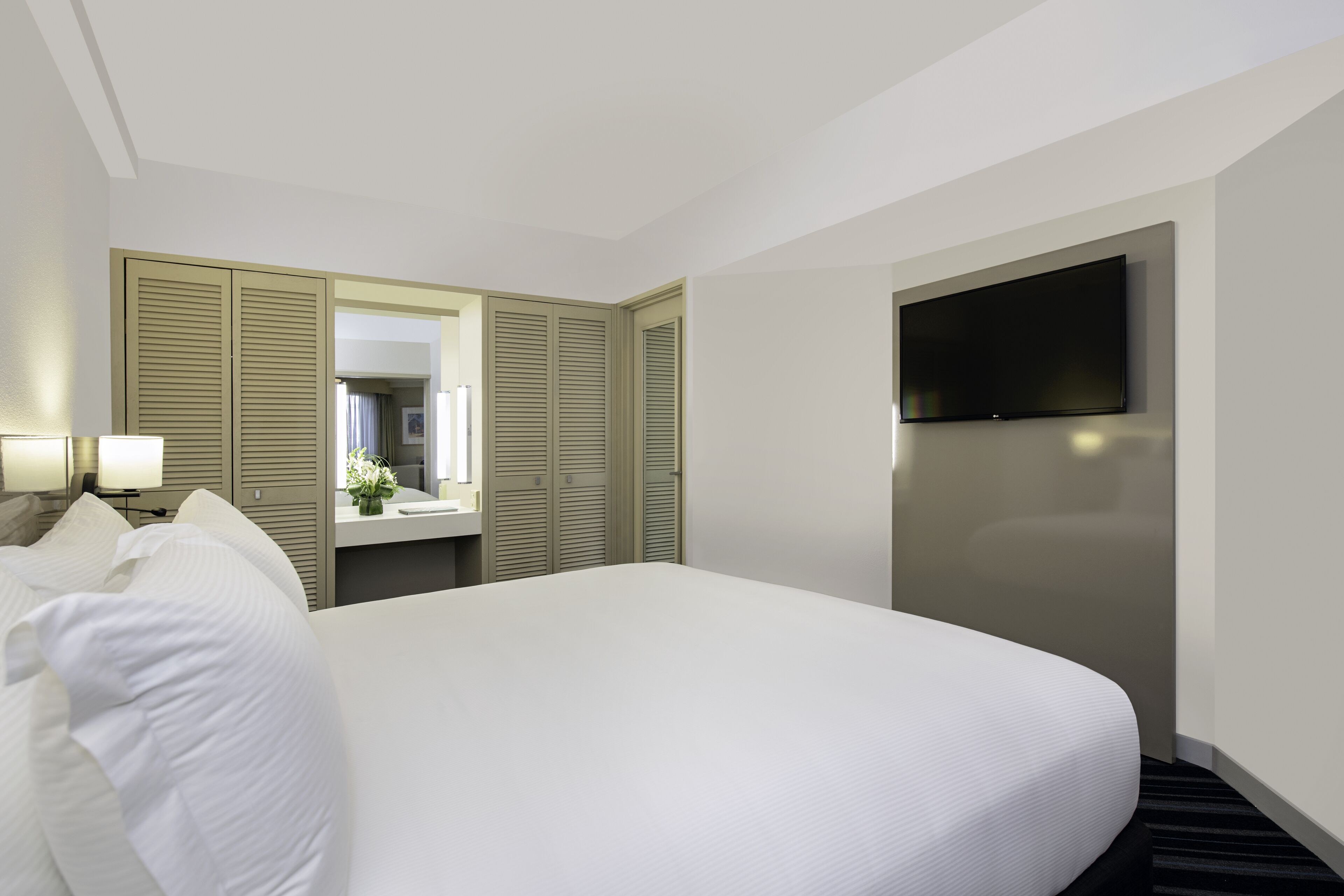 Quarto de hotel com uma cama grande, televisão de tela plana na parede e uma janela com persianas.