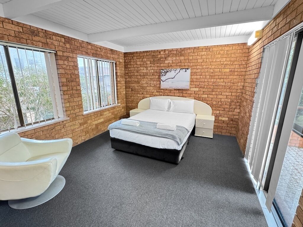 Quarto com parede de tijolos, cama, cadeira e janela.