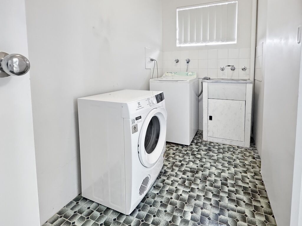 Uma lavanderia compacta com máquina de lavar, pia e armário.