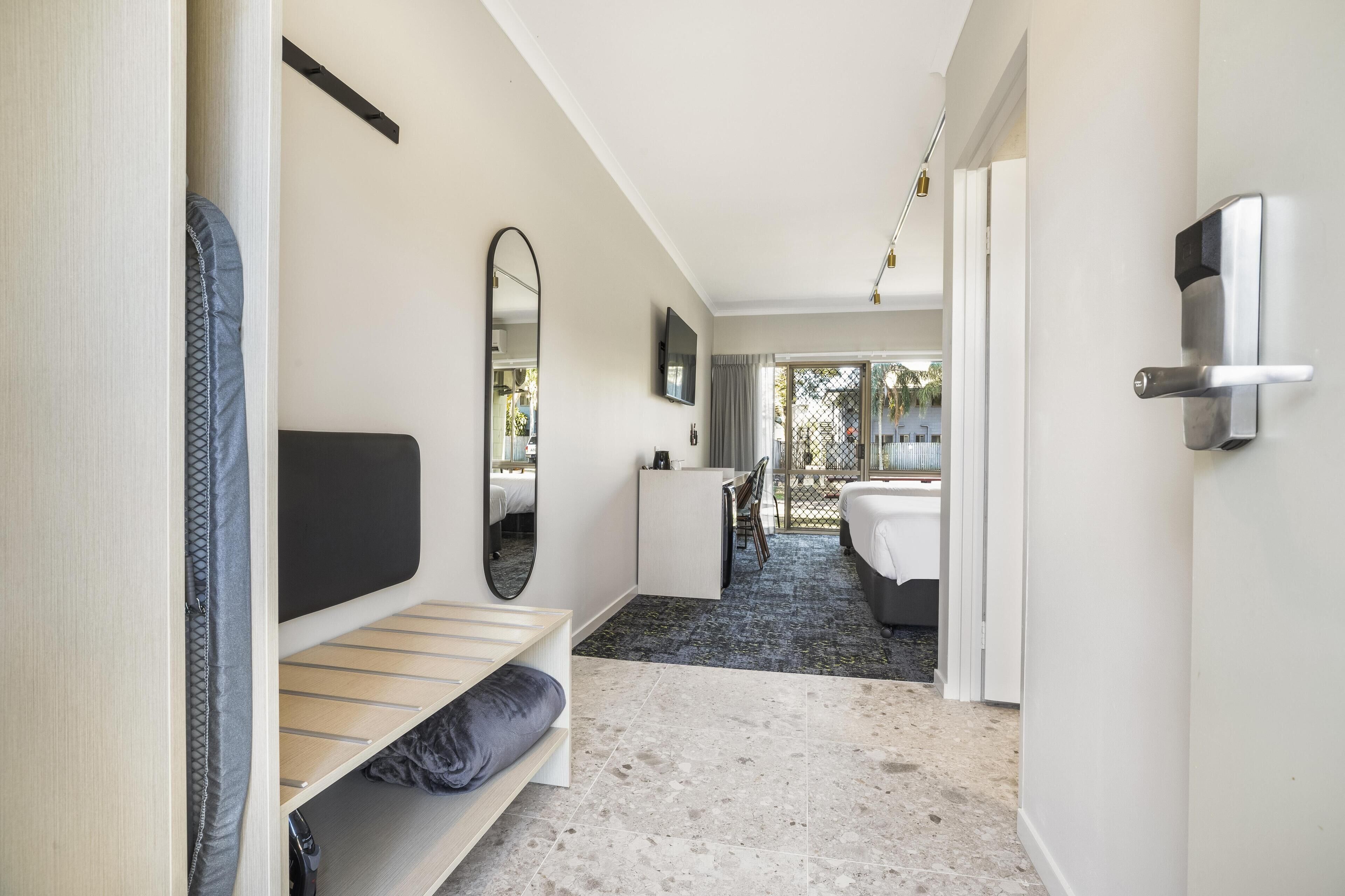 Quarto de hotel moderno com cama, um banco, espelho, TV e banheiro visível através de uma porta aberta.