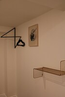 Quarto com um cabide preto, um quadro emoldurado e uma prateleira de arame.