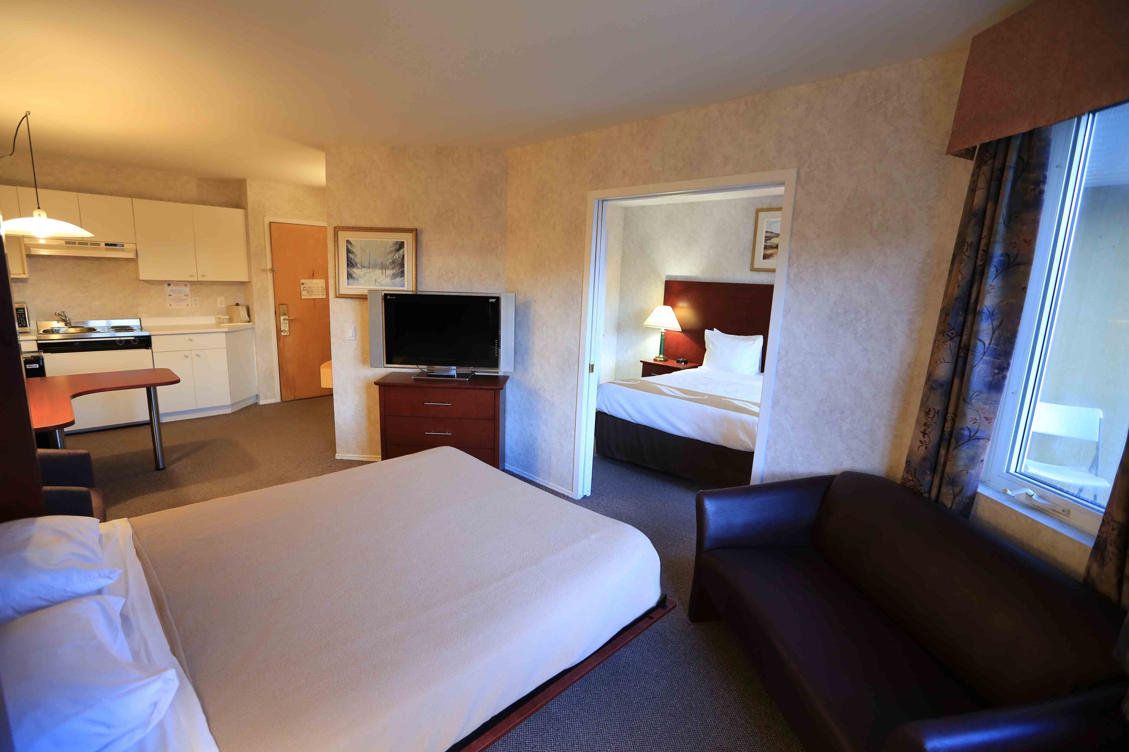 Quarto de hotel com uma cama grande, um sofá, uma televisão, uma escrivaninha e uma cozinha compacta.