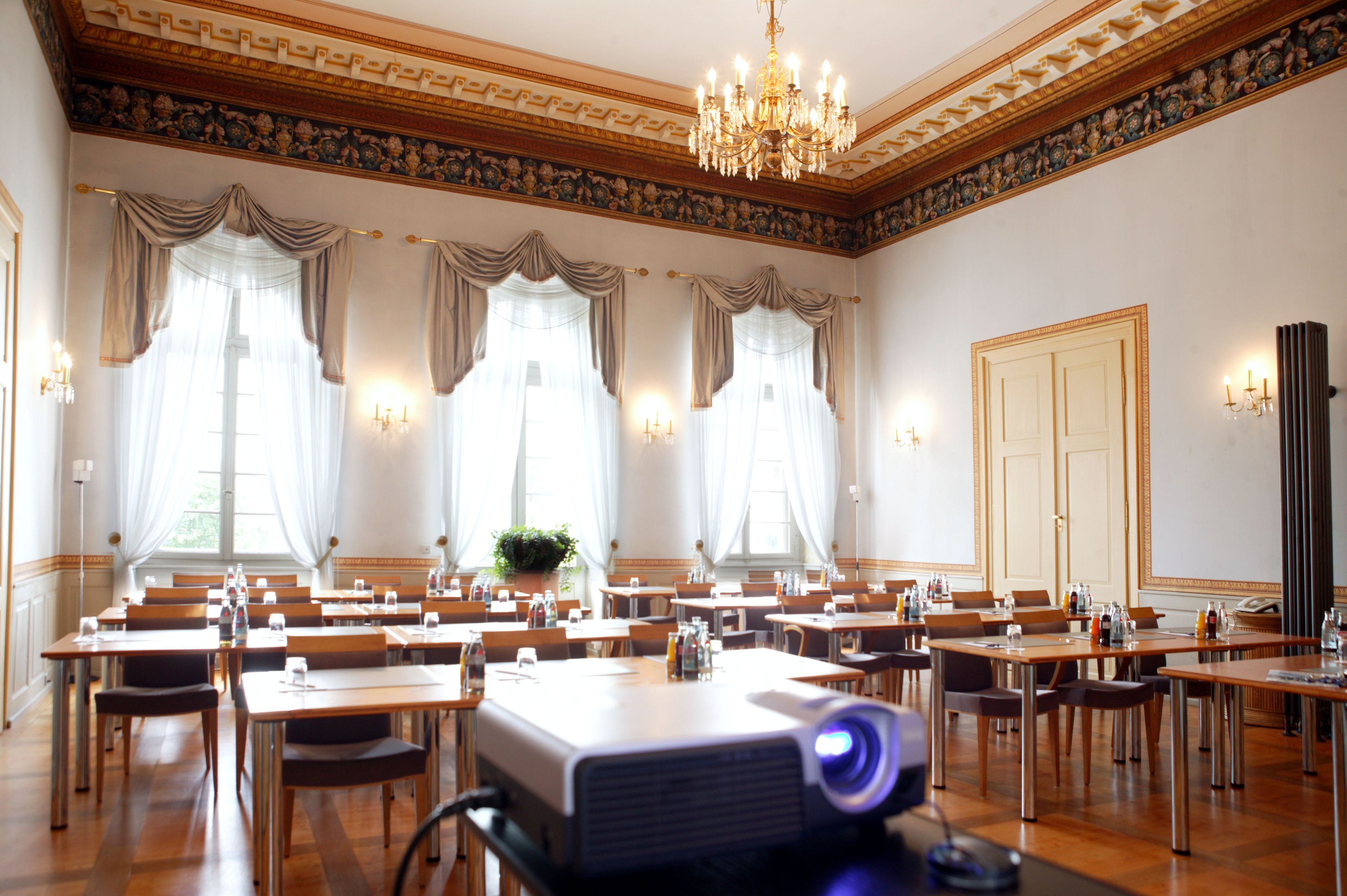 Uma sala de conferências com várias mesas e cadeiras, um projetor e um candelabro.