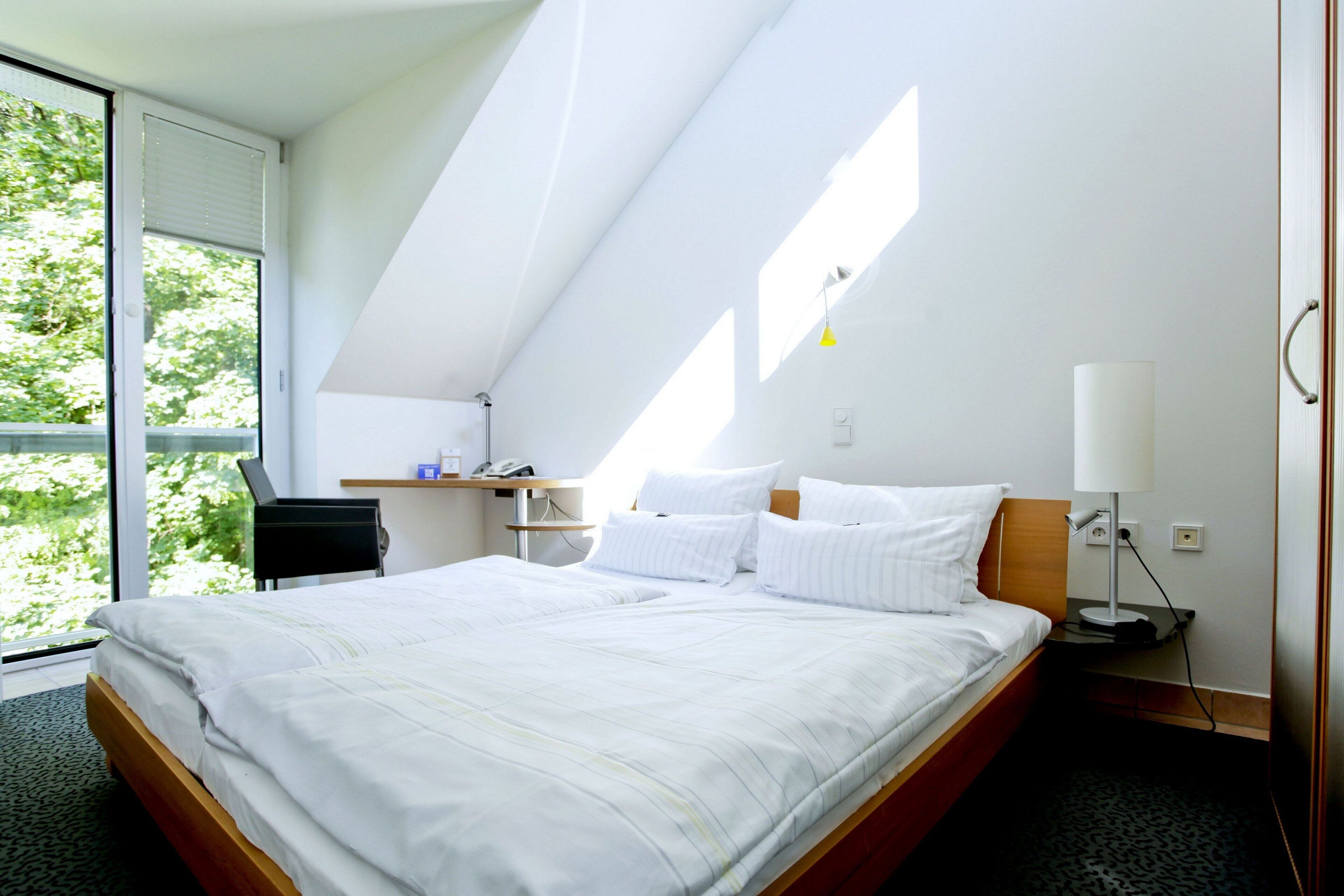 Quarto de hotel moderno com uma cama grande, uma escrivaninha e vista para o verde lá fora.