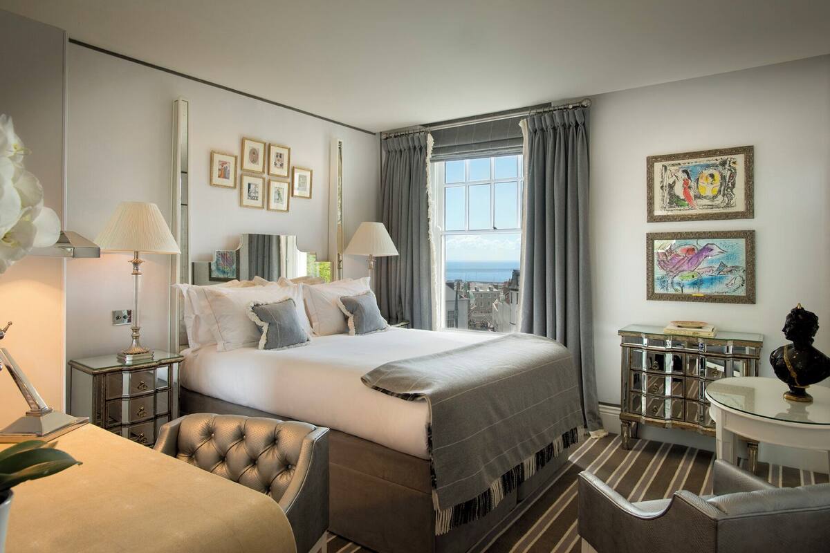 Quarto de hotel com cama, mesas de cabeceira, escrivaninha, uma cadeira e obras de arte nas paredes.