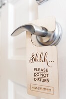 Um sino de madeira com uma placa que diz "Silêncio... POR FAVOR, NÃO ATRAPALHE" e "Cape Town Hollow Boutique Hotel" abaixo.