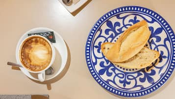 Uma mesa com uma xícara de café, um prato com pão, um copo de suco de laranja e uma pequena tigela de molho.