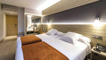 Quarto de hotel com cama, mesa de cabeceira, espelho e cabeceira de madeira.