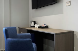 Quarto de hotel com uma mesa, uma cadeira, chaleira, telefone e um pequeno tabuleiro preto com objetos.